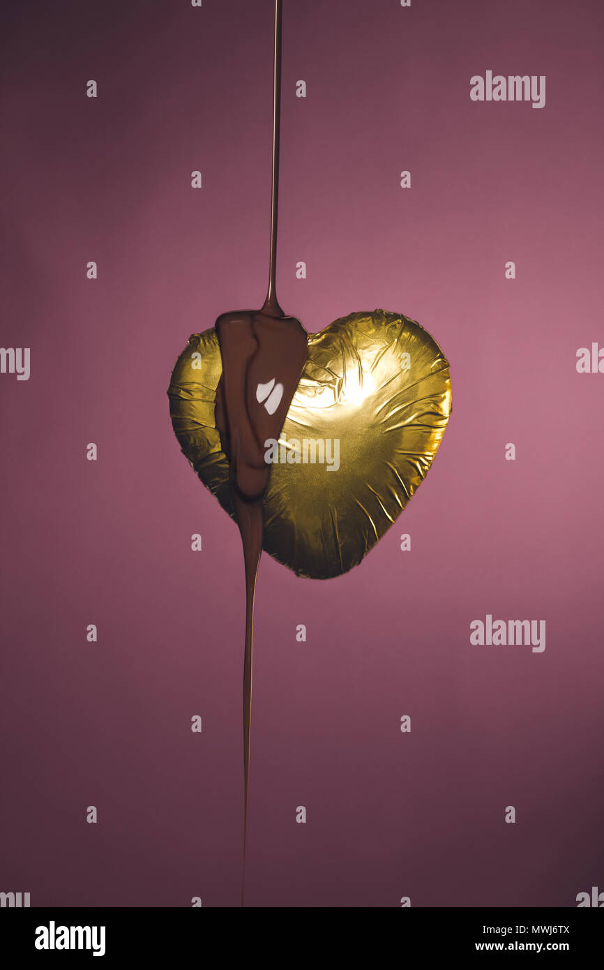 heart shaped candy in golden wrapper with pouring liquid chocolate ...