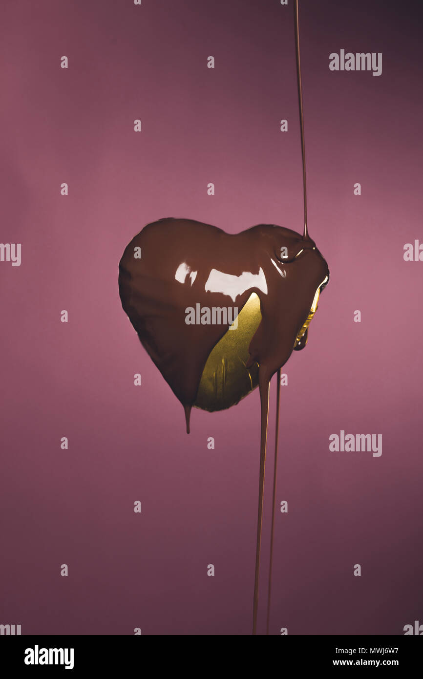 heart shaped candy in golden wrapper with pouring liquid chocolate ...