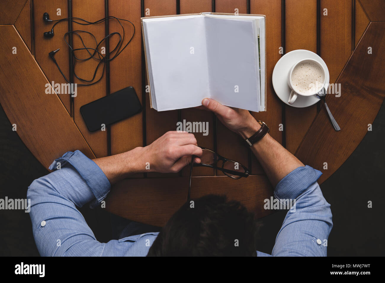 overhead view of man reading book at wooden table during coffee break ...