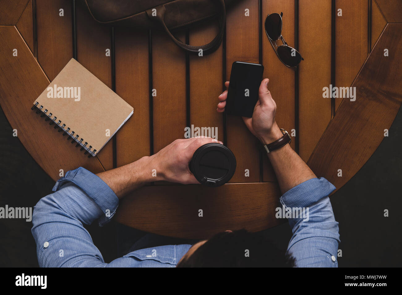 overhead view of man with coffee to go using smartphone at wooden table ...