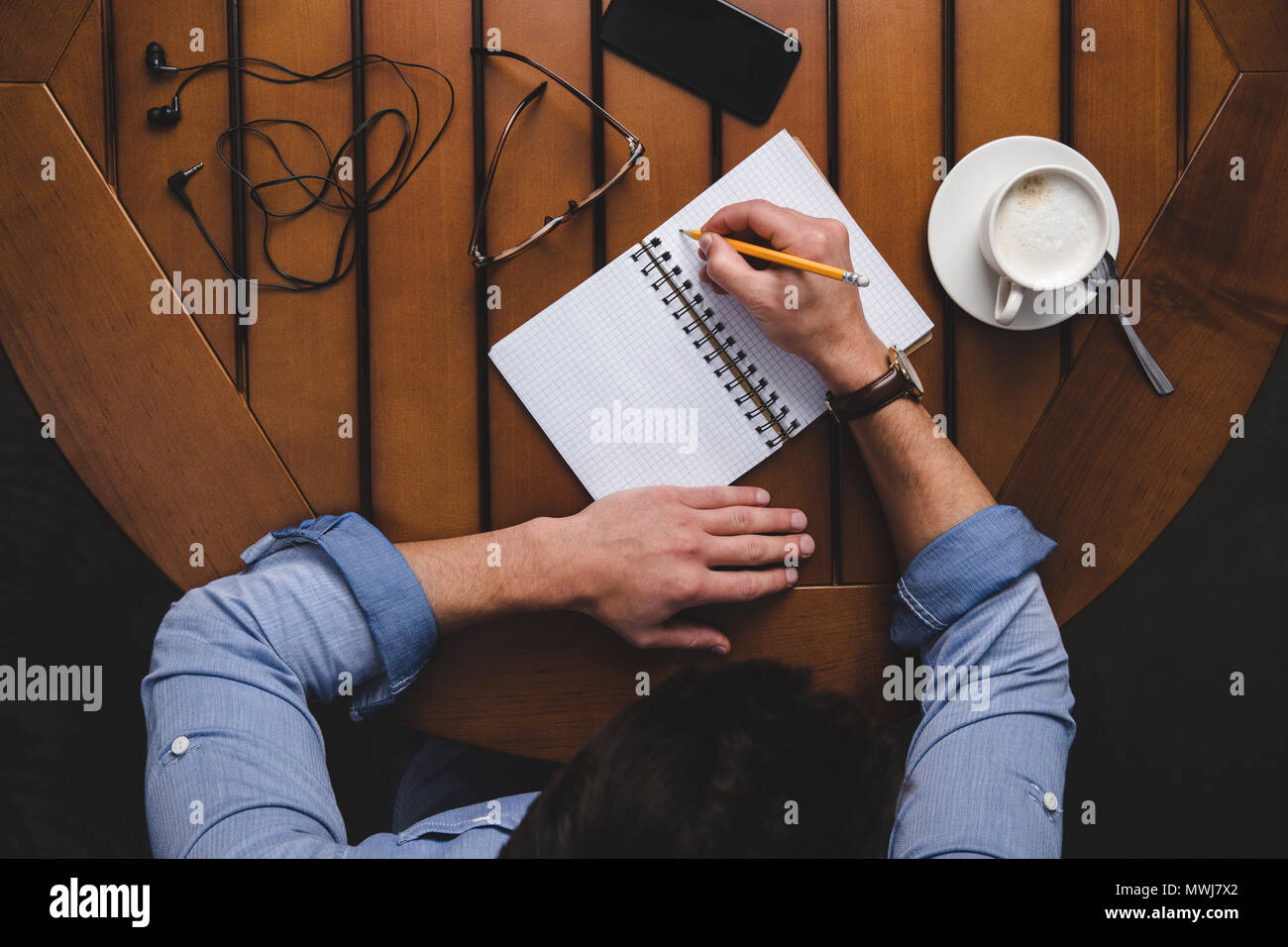 overhead view of man writing in notepad at wooden table Stock Photo - Alamy