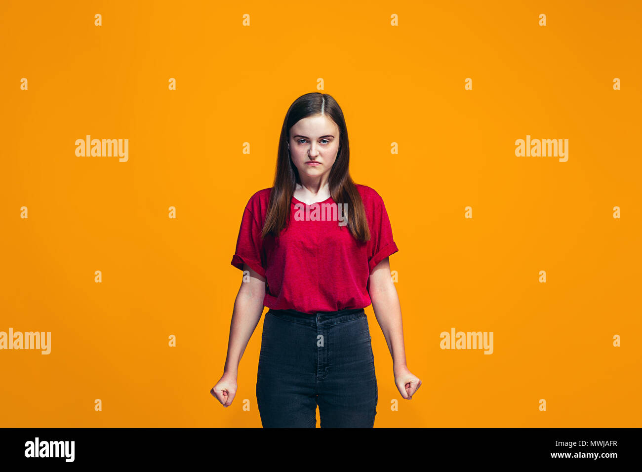 Portrait of angry teen girl on a orange studio background Stock Photo ...