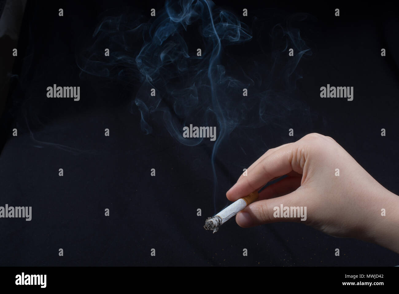 Hand is holding smoking cigarette with smoke around Stock Photo - Alamy