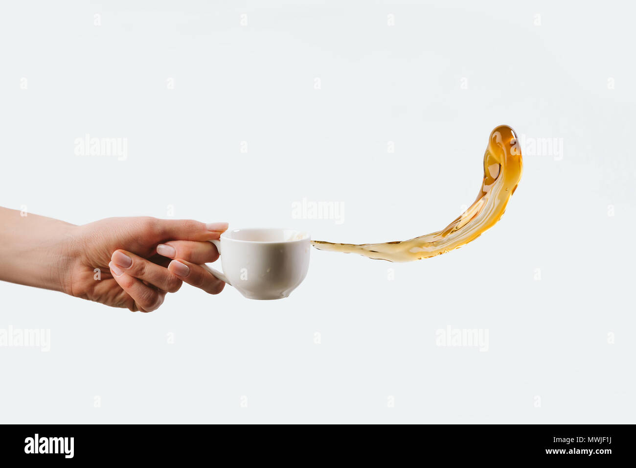 cropped view of hand holding white cup with splash of aromatic coffee ...