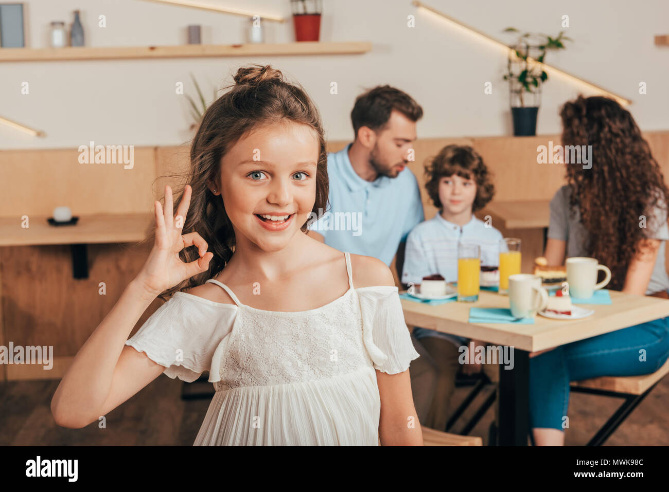 little girl showing okay sign in cafe with her happy family blurred on ...