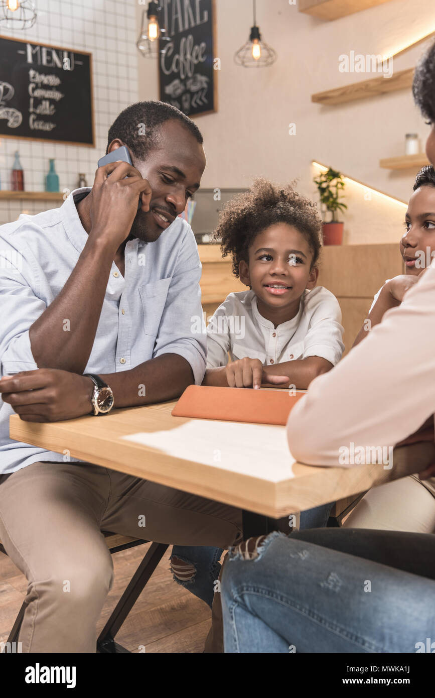 african-american family sitting in cafe while father talking by phone ...