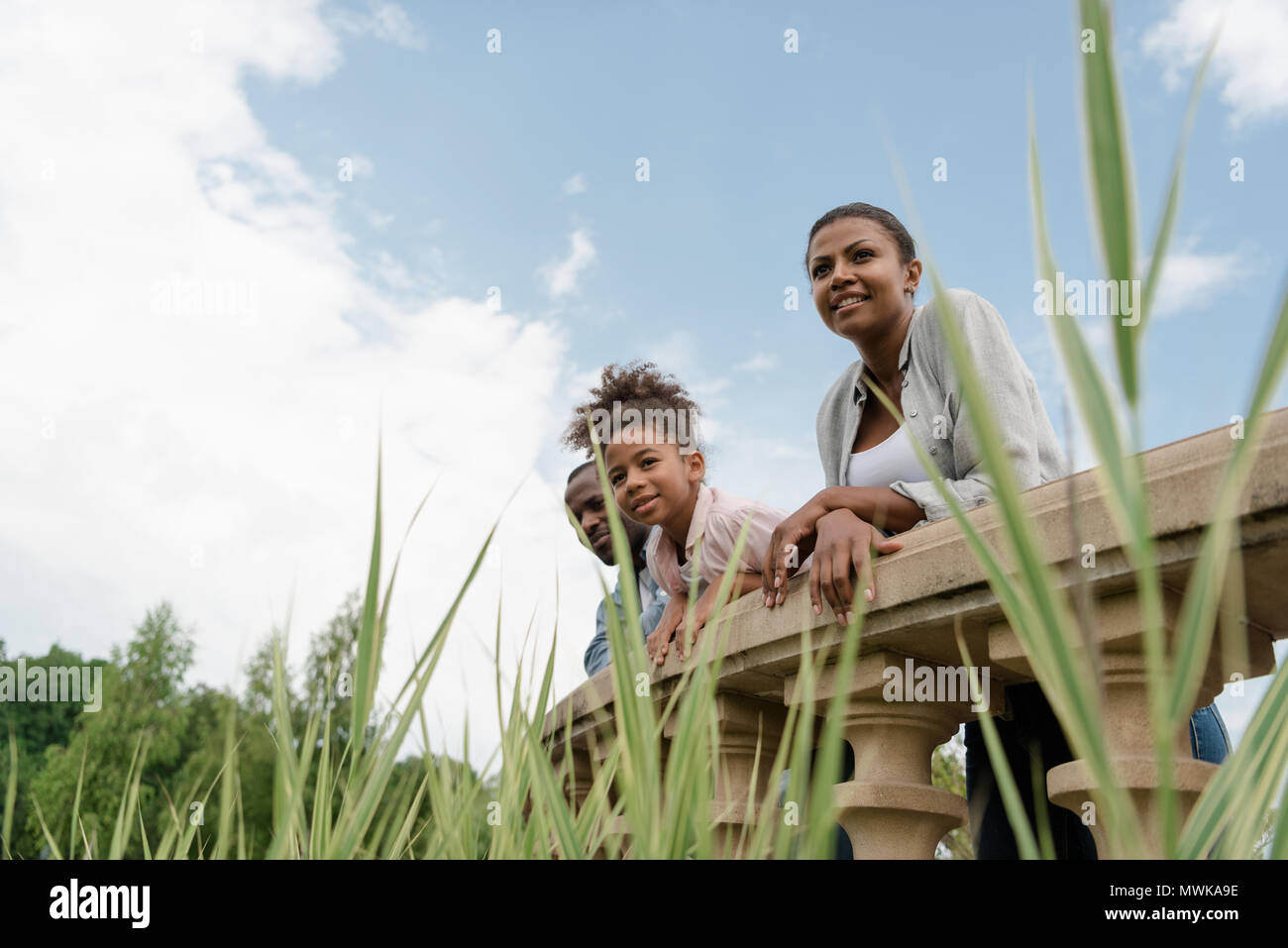 african american little girl and parents standing on bridge together in ...