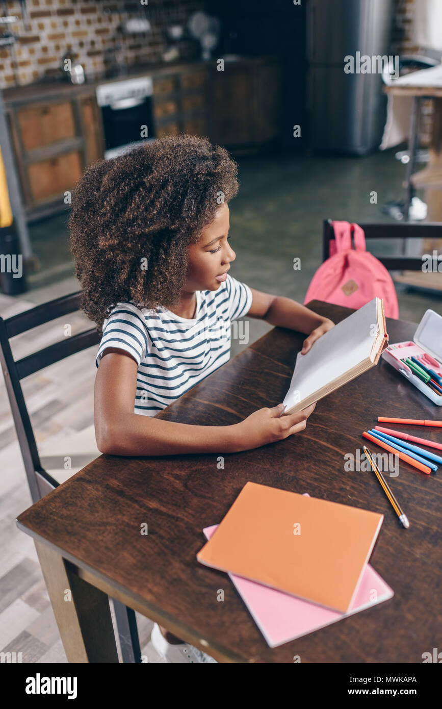 Little girl reading a book at the kitchen table Stock Photo - Alamy