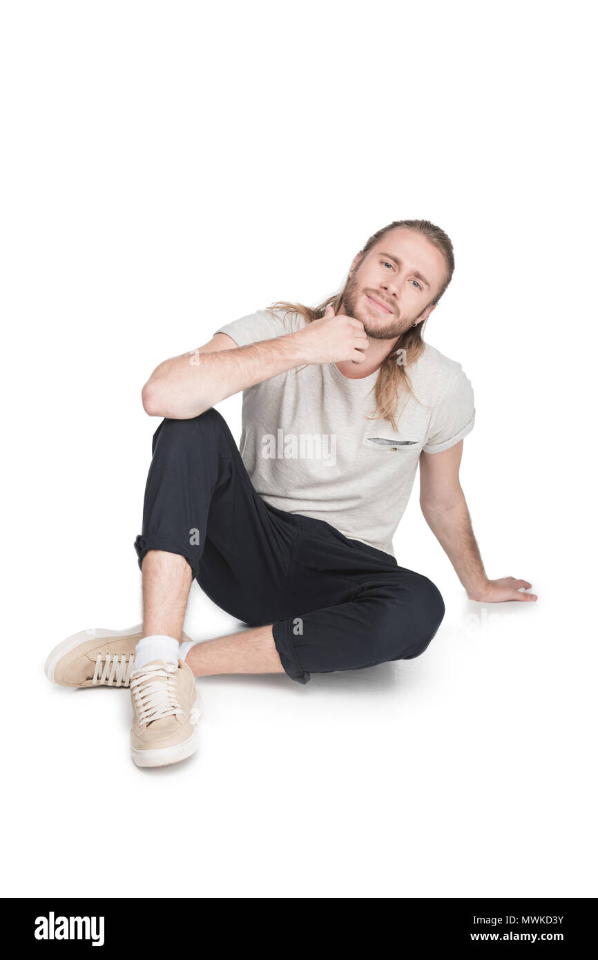 young pensive man sitting and looking at camera, isolated on white ...