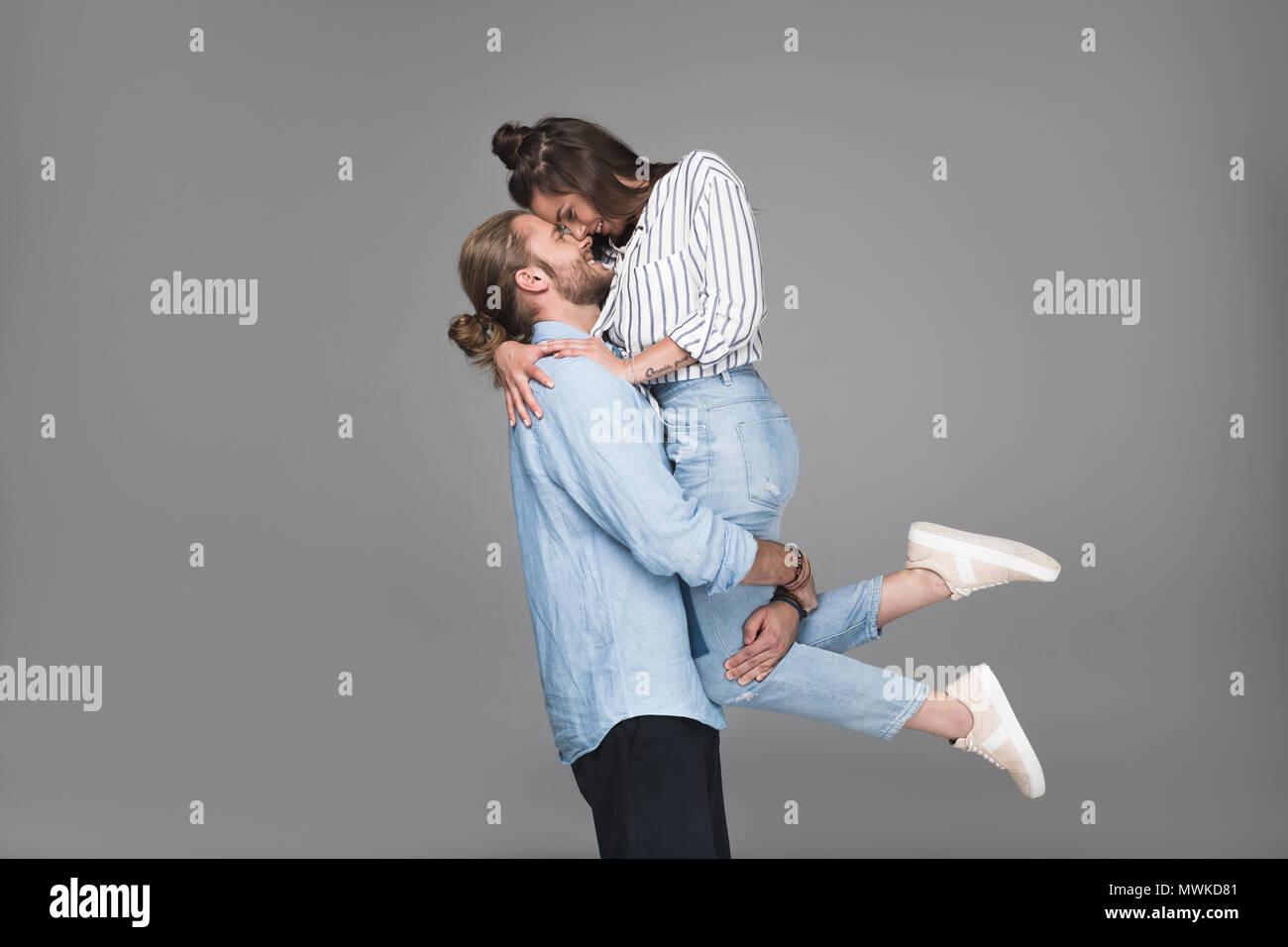 Happy young man carrying and hugging beautiful girl isolated on grey ...