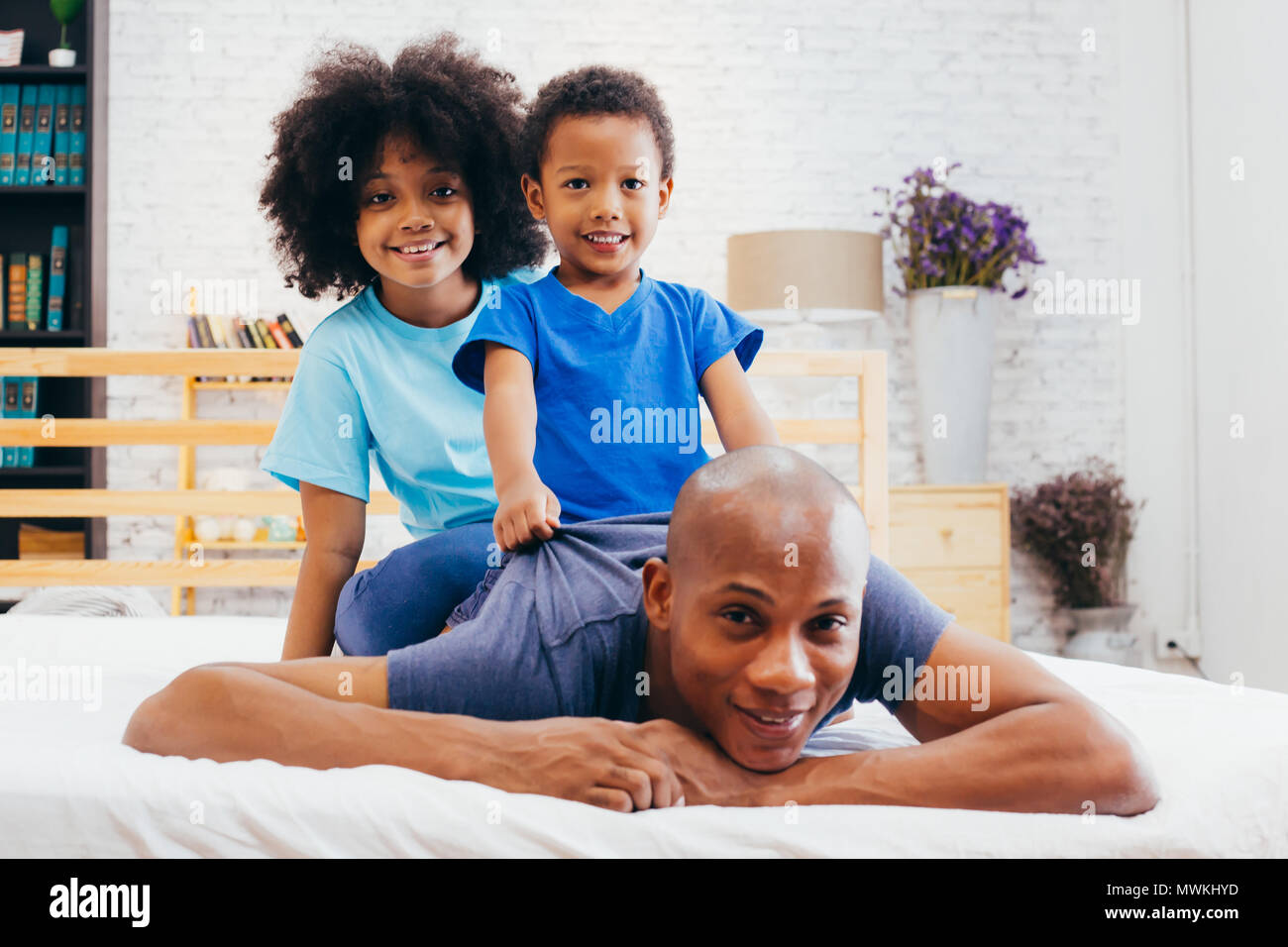 African American family of three, kids sitting on father's back at home ...
