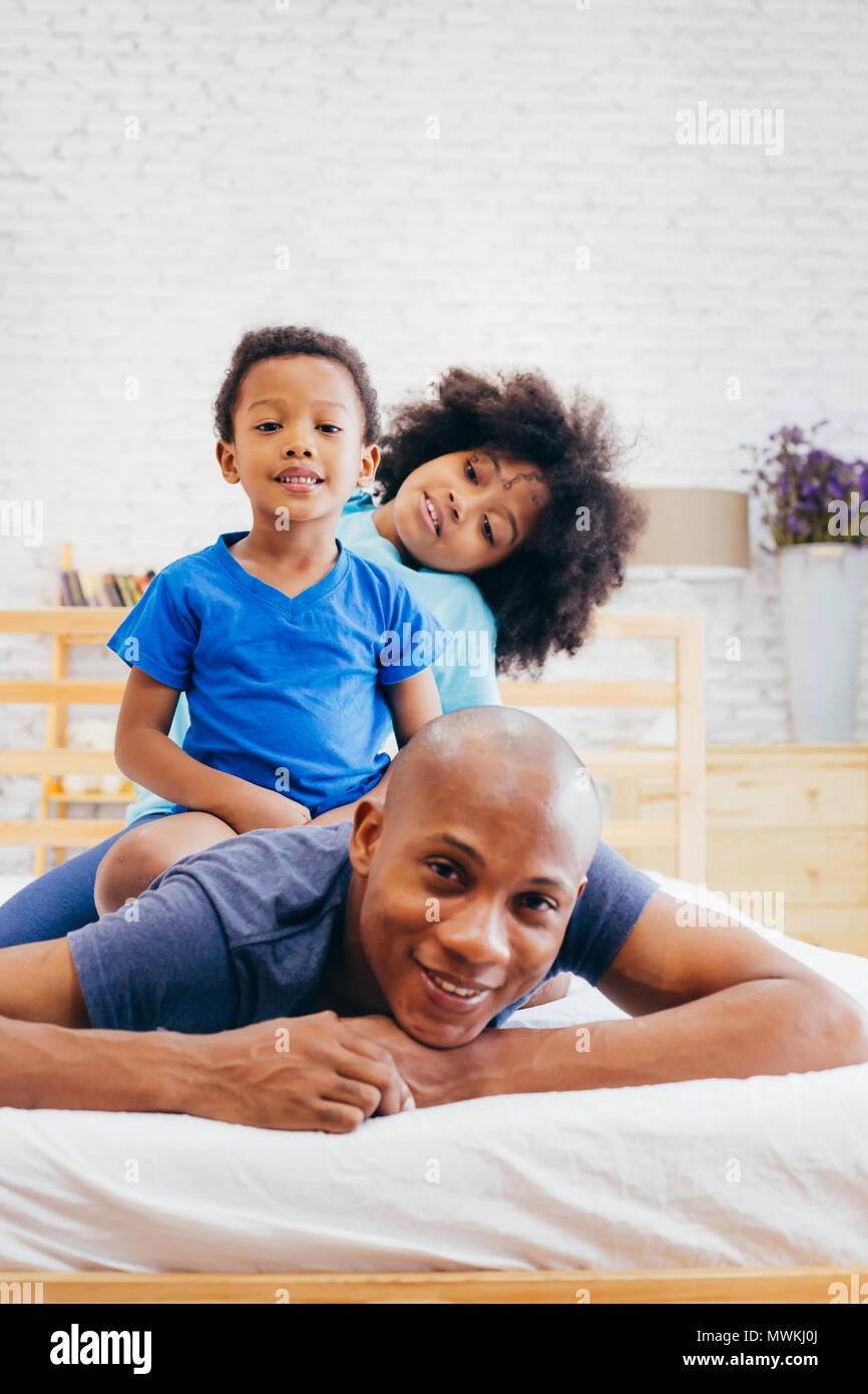 African American family of three, kids sitting on father's back at home ...