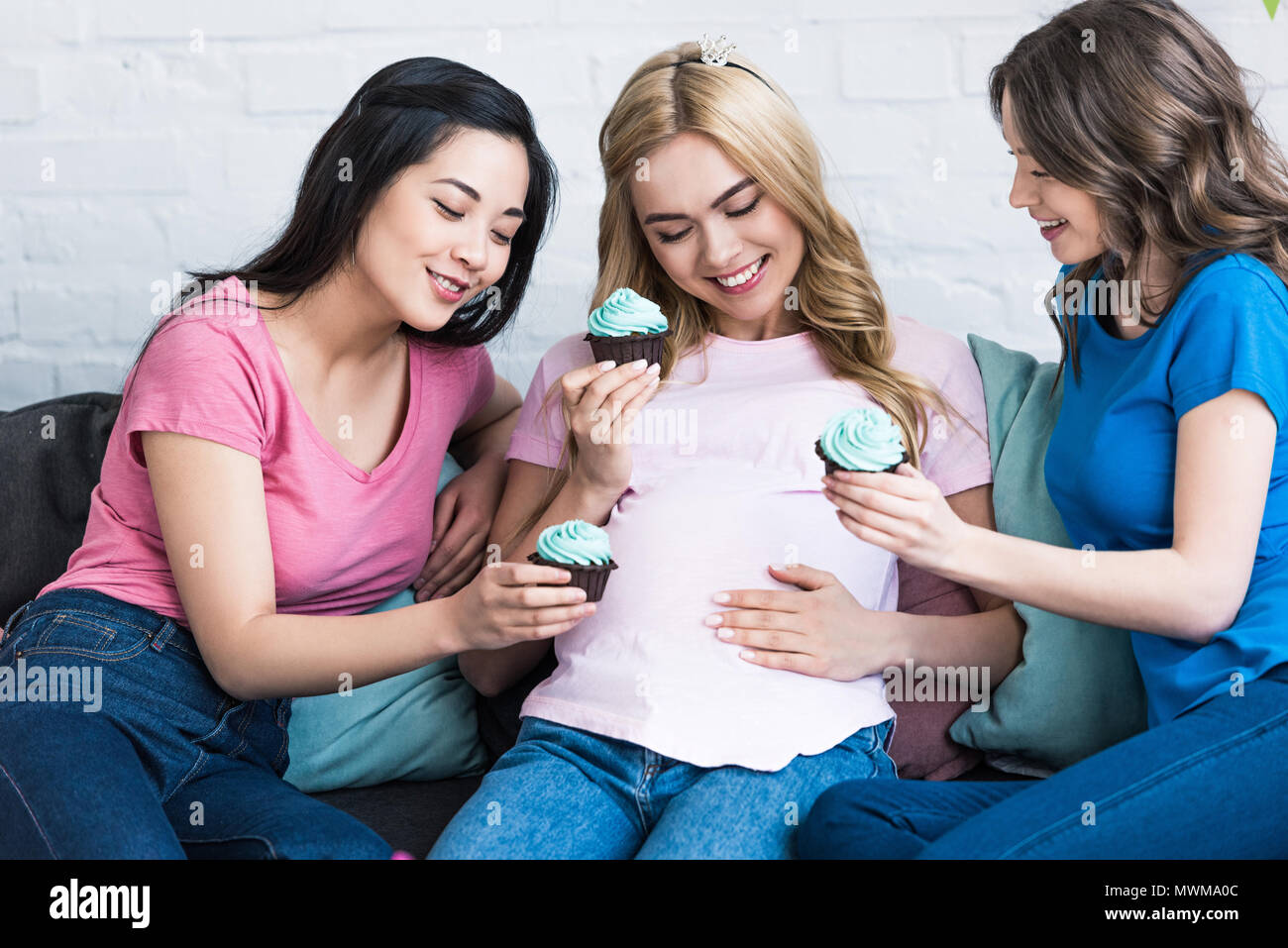 happy multicultural friends and pregnant woman with cupcakes at baby ...