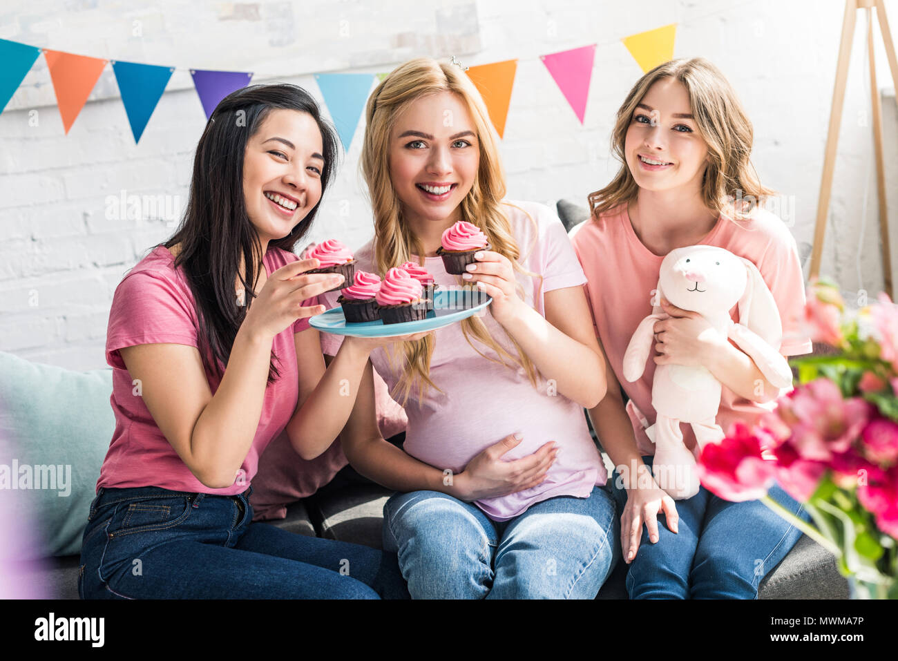 multicultural friends and pregnant woman eating pink cupcakes at baby ...