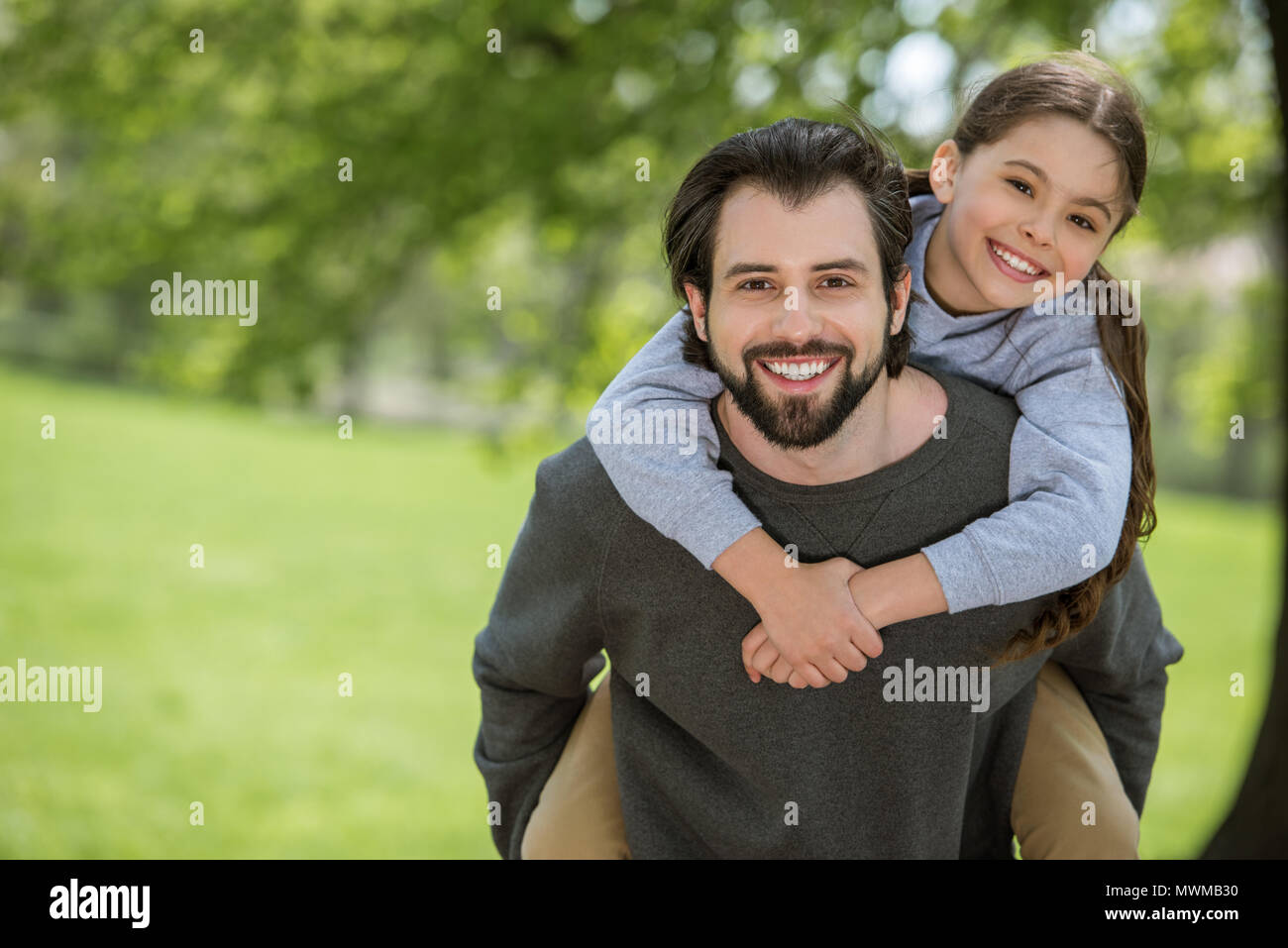 smiling father doing piggyback ride to daughter in park Stock Photo - Alamy