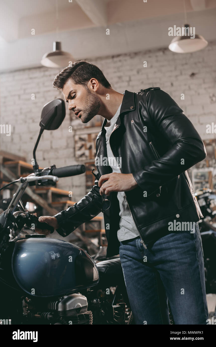 young handsome biker in black leather jacket with classic motorcycle in ...