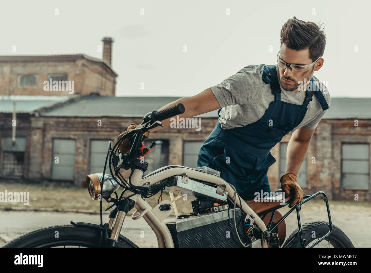 mechanic in goggles repairing vintage motorcycle standing outside at ...