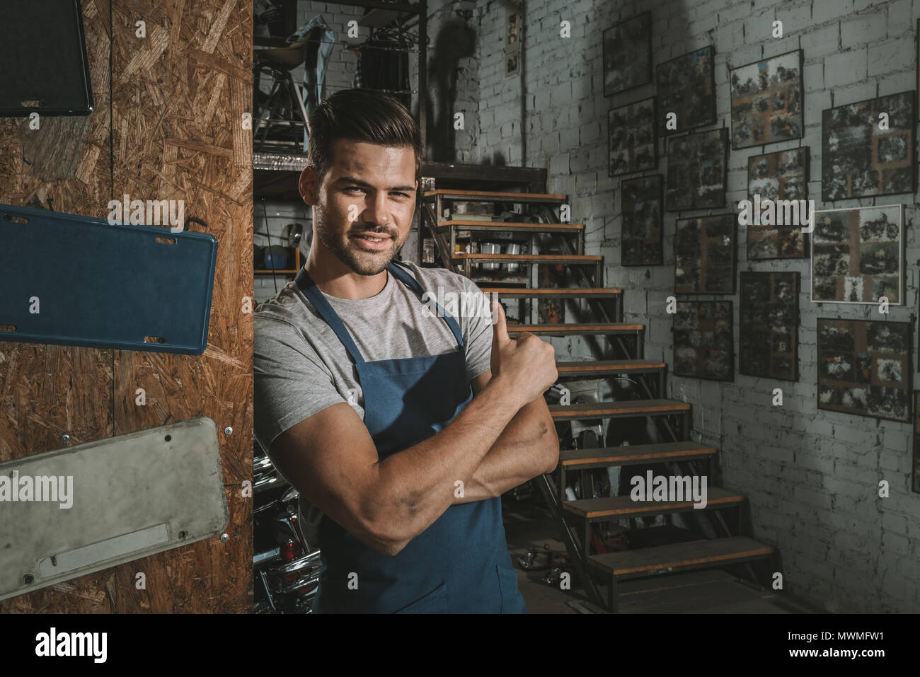 male mechanic with thumb up in repair shop with number plates on wall ...