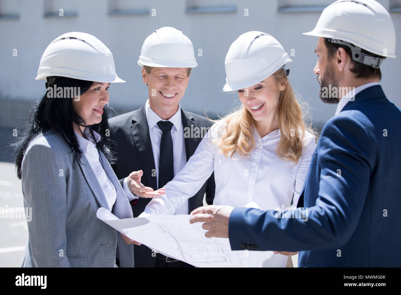 Professional team of smiling architects in hard hats working together ...