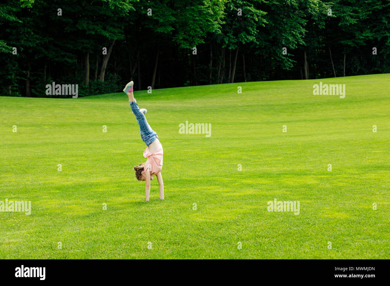 full length view of cute little girl performing handstand on green ...