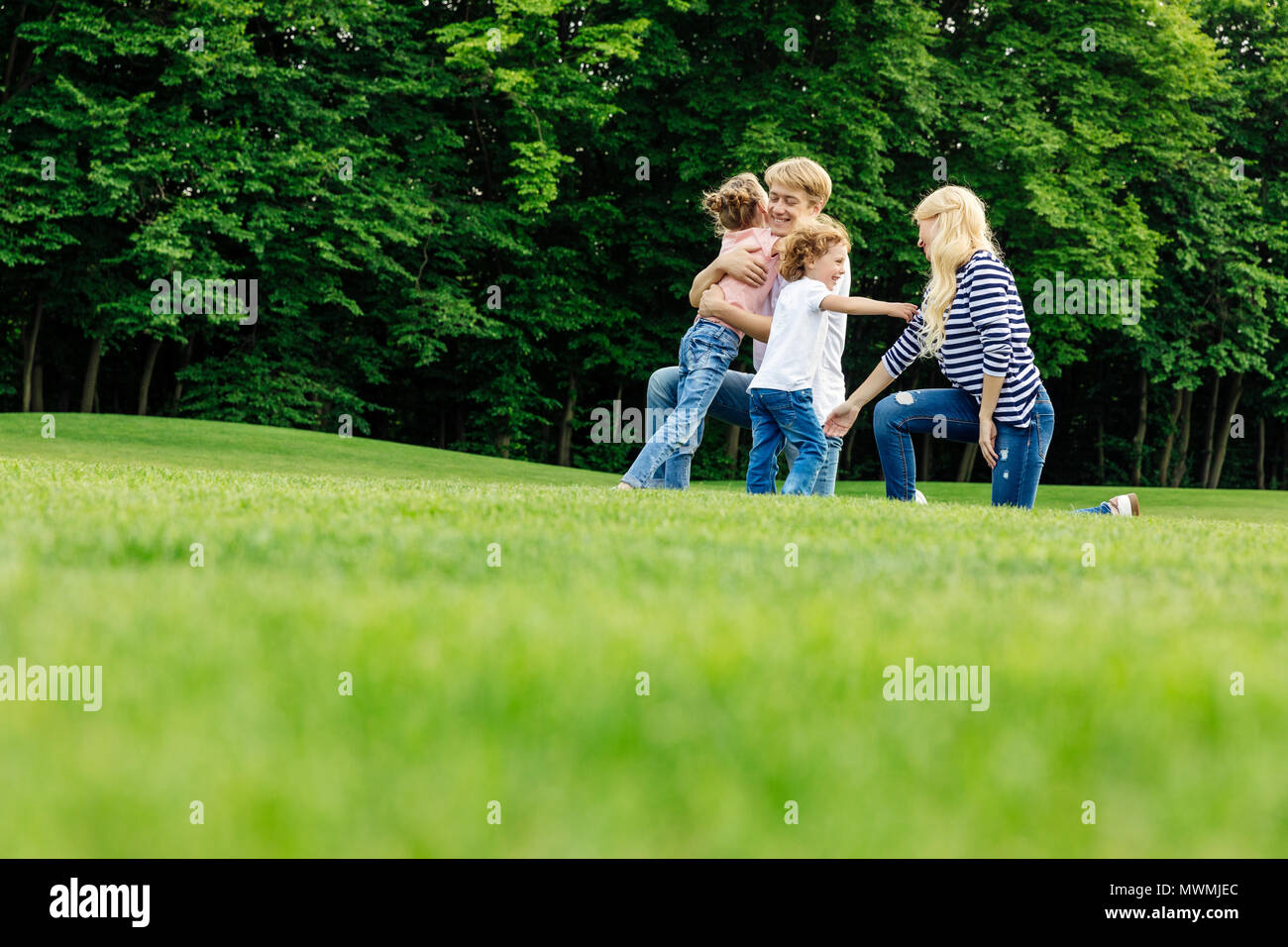 happy young family with two children hugging on green meadow in park ...