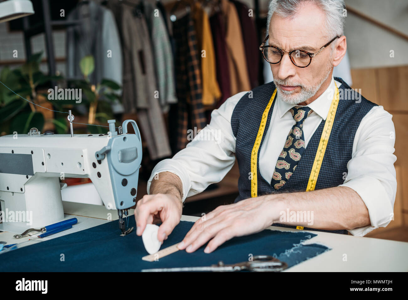 senior tailor making pattern on cloth with piece of chalk at sewing ...