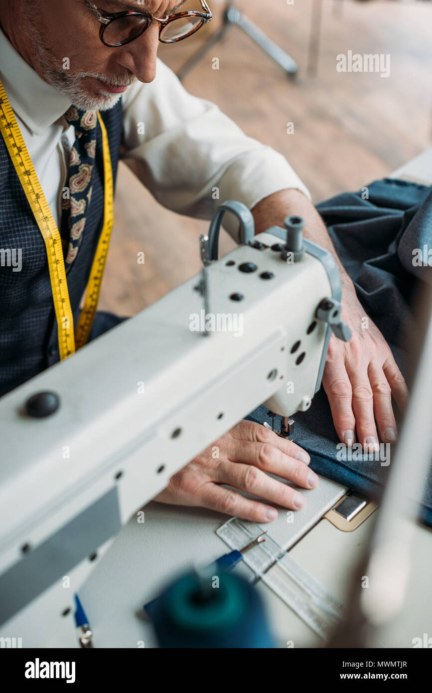 handsome professional tailor sewing cloth with sewing machine at sewing ...