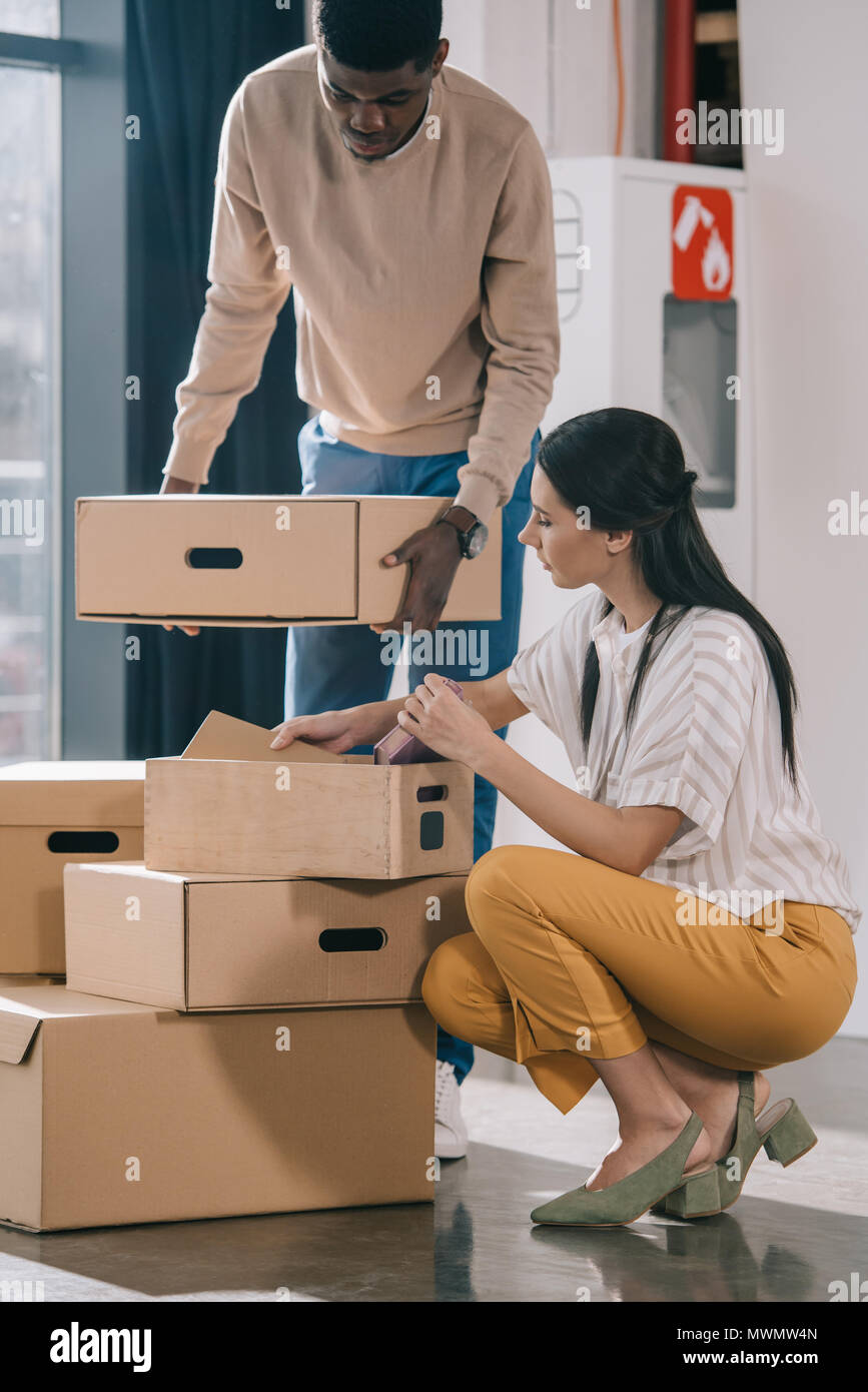 young multiethnic coworkers unpacking cardboard boxes during relocation ...