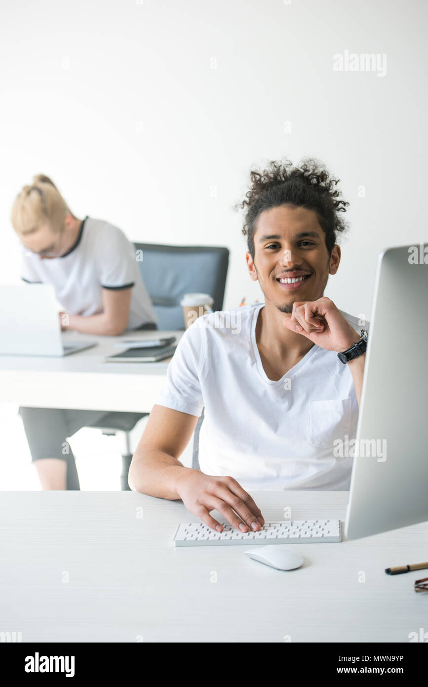 handsome young african american man using desktop computer and smiling at camera in office Stock ...