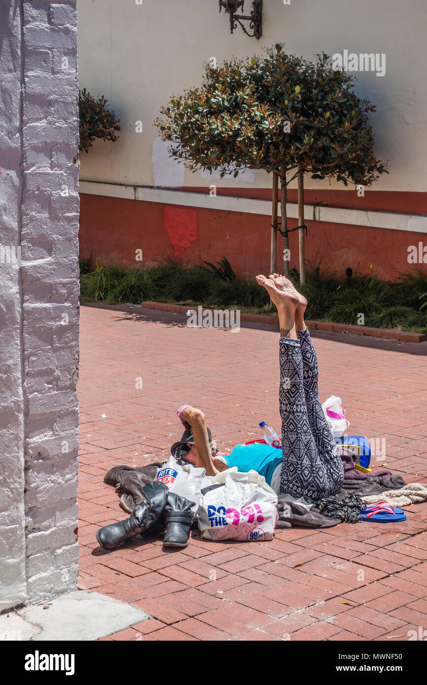 An older adult female homeless person lies on the city sidewalk and ...