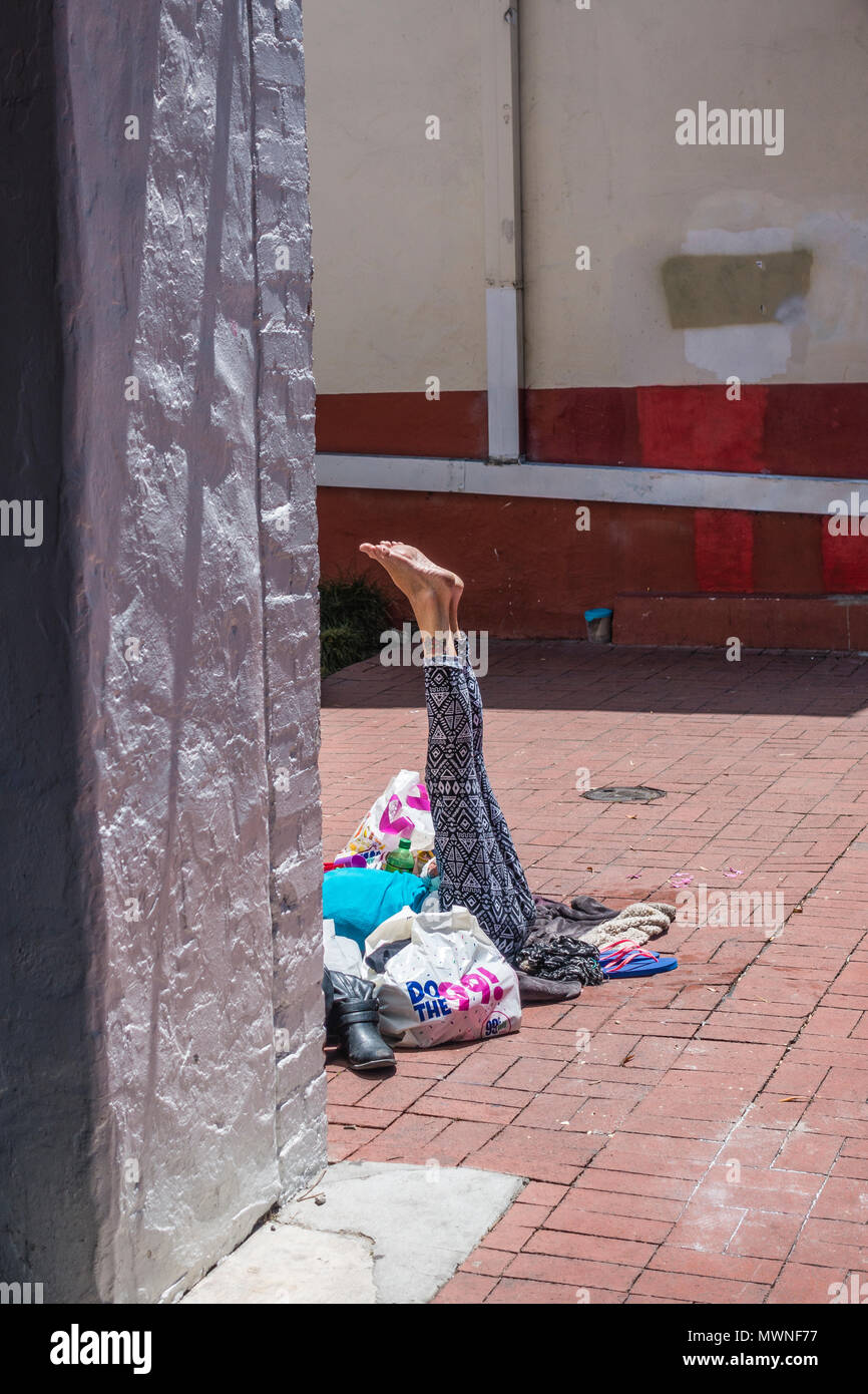 An older adult female homeless person lies on the city sidewalk and ...