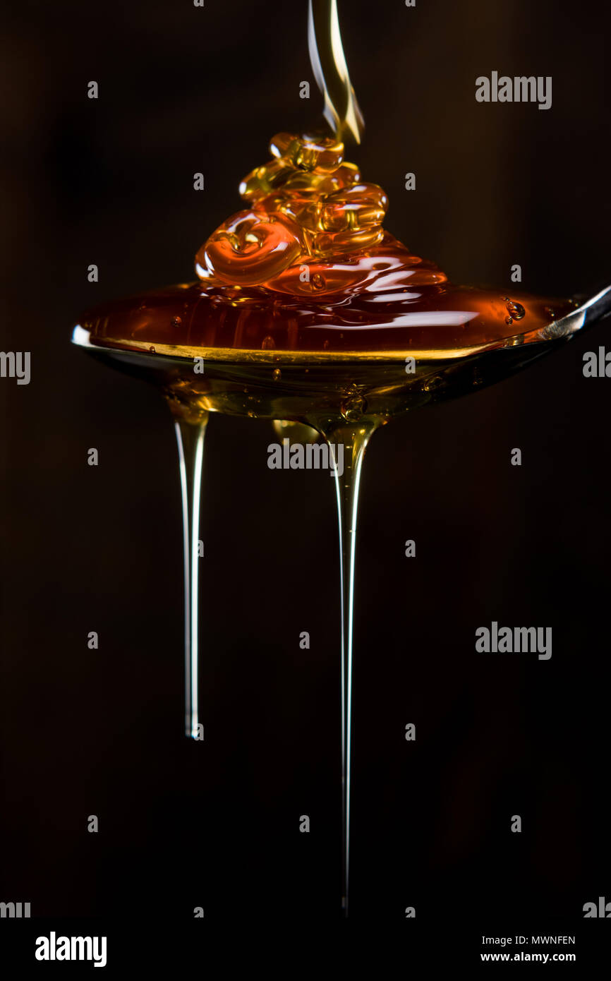 Strands of Honey Drip from Overflowing Spoon with dark background Stock ...