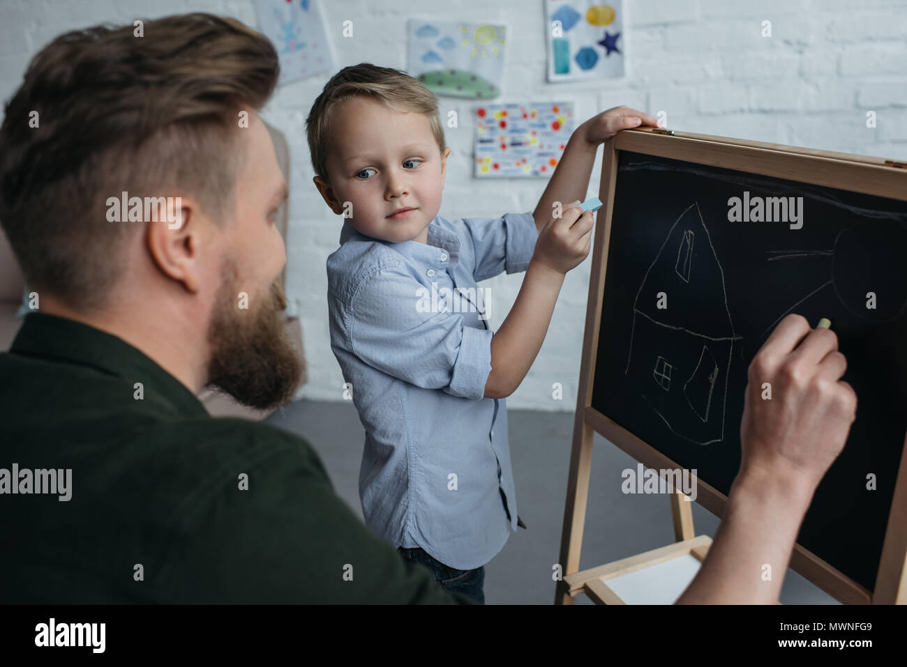 side view of little boy and father with pieces of chalk drawing picture ...