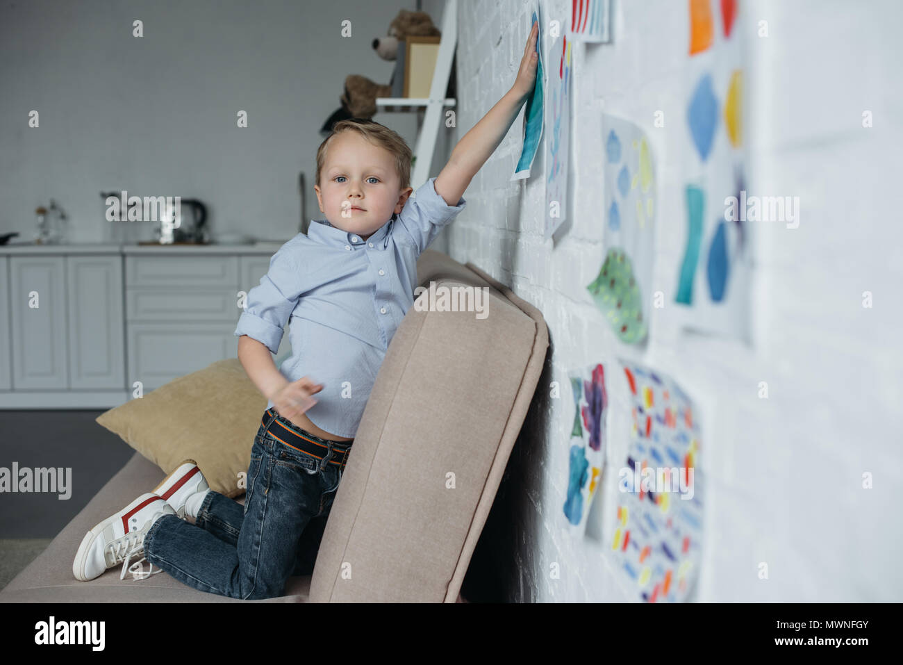 side view of little kid hanging childish pictures on wall at home Stock ...