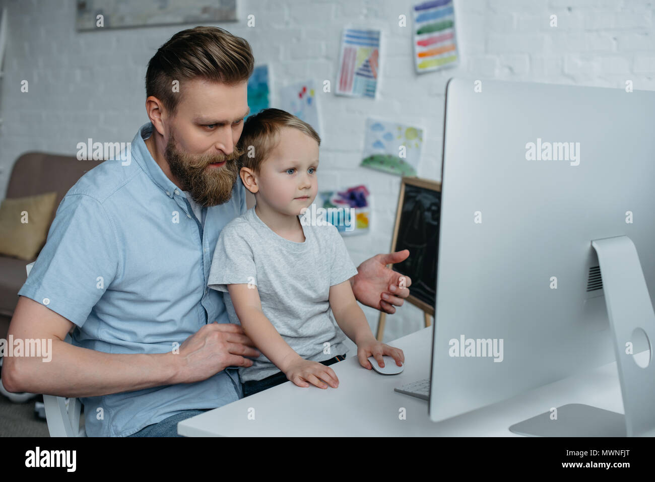 father and little son looking at computer screen while using computer ...