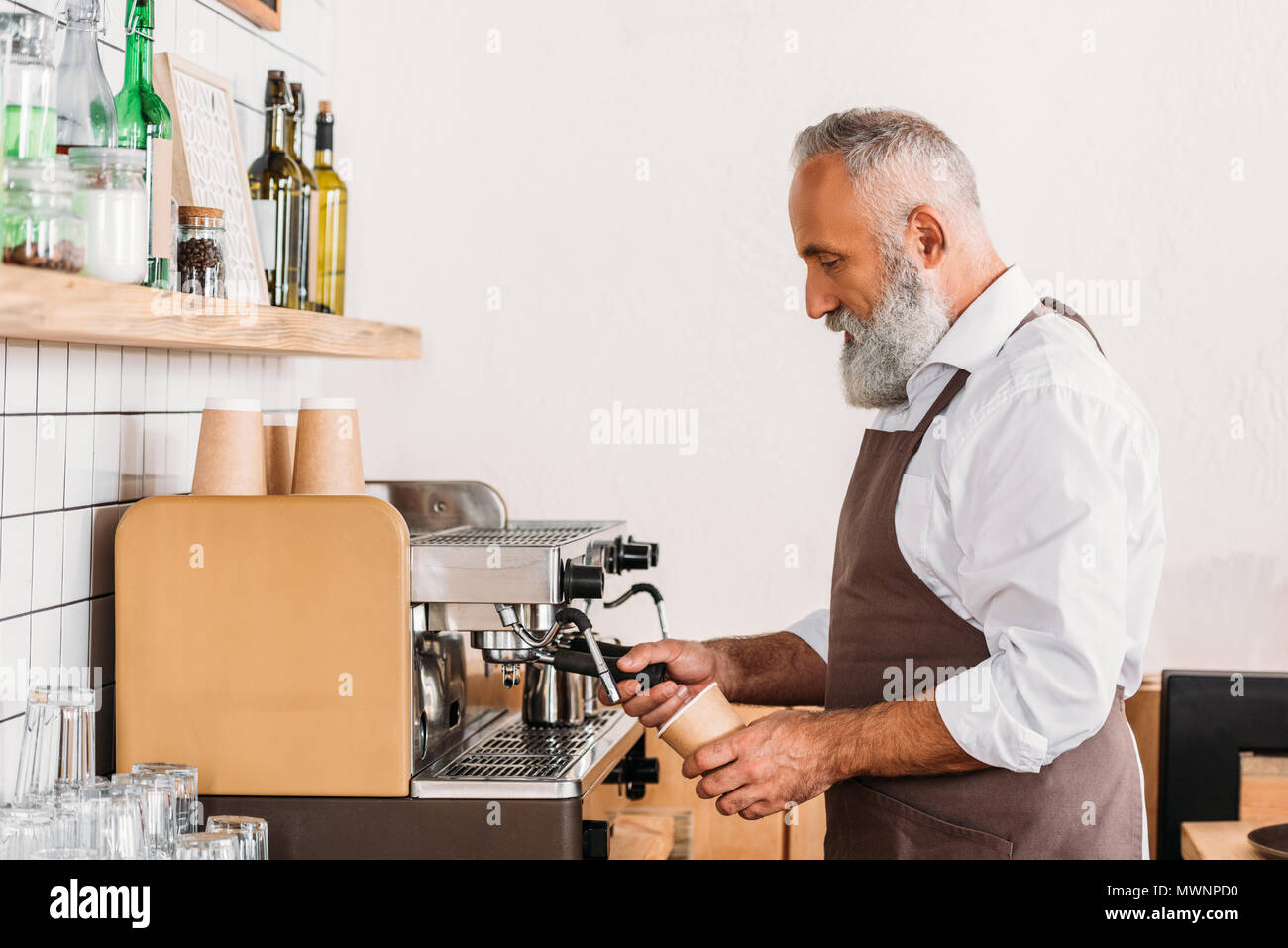 side view of focused senior barista using coffee machine while making ...