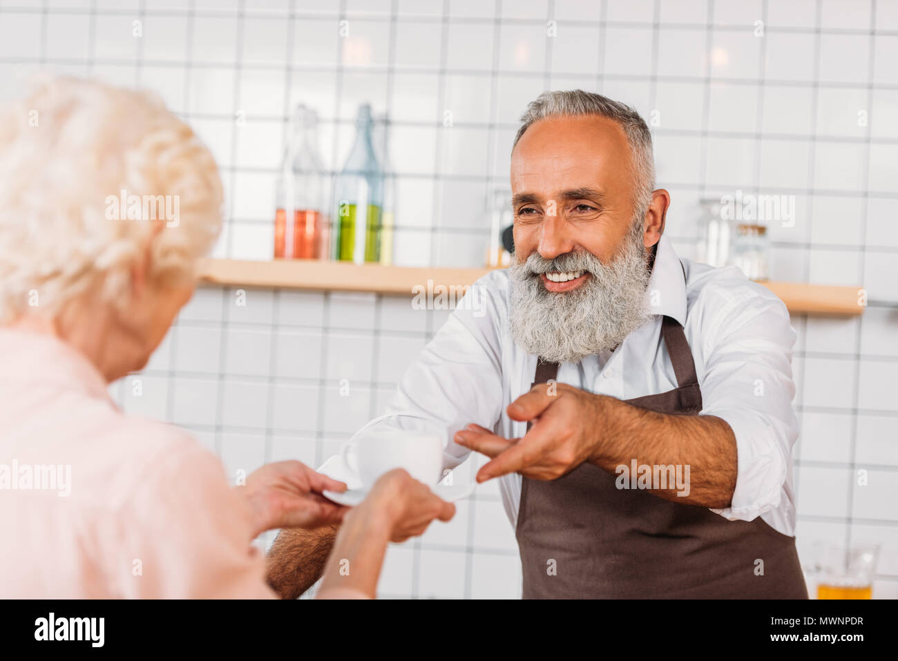 selective focus of smiling senior barista serving cup of coffee to ...