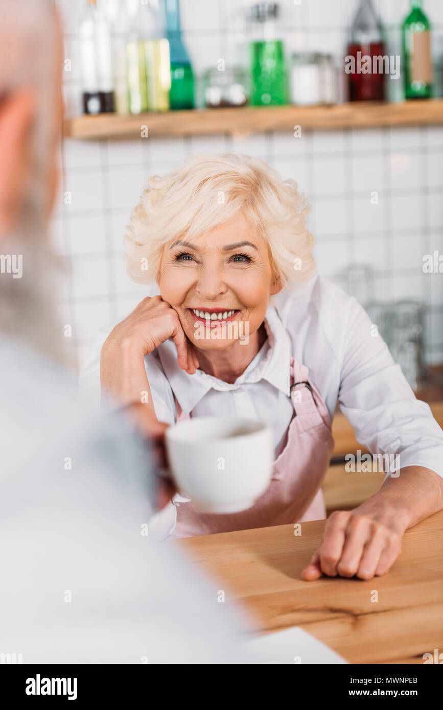 selective focus of cheerful barista in apron looking at visitor at counter in cafe Stock Photo ...