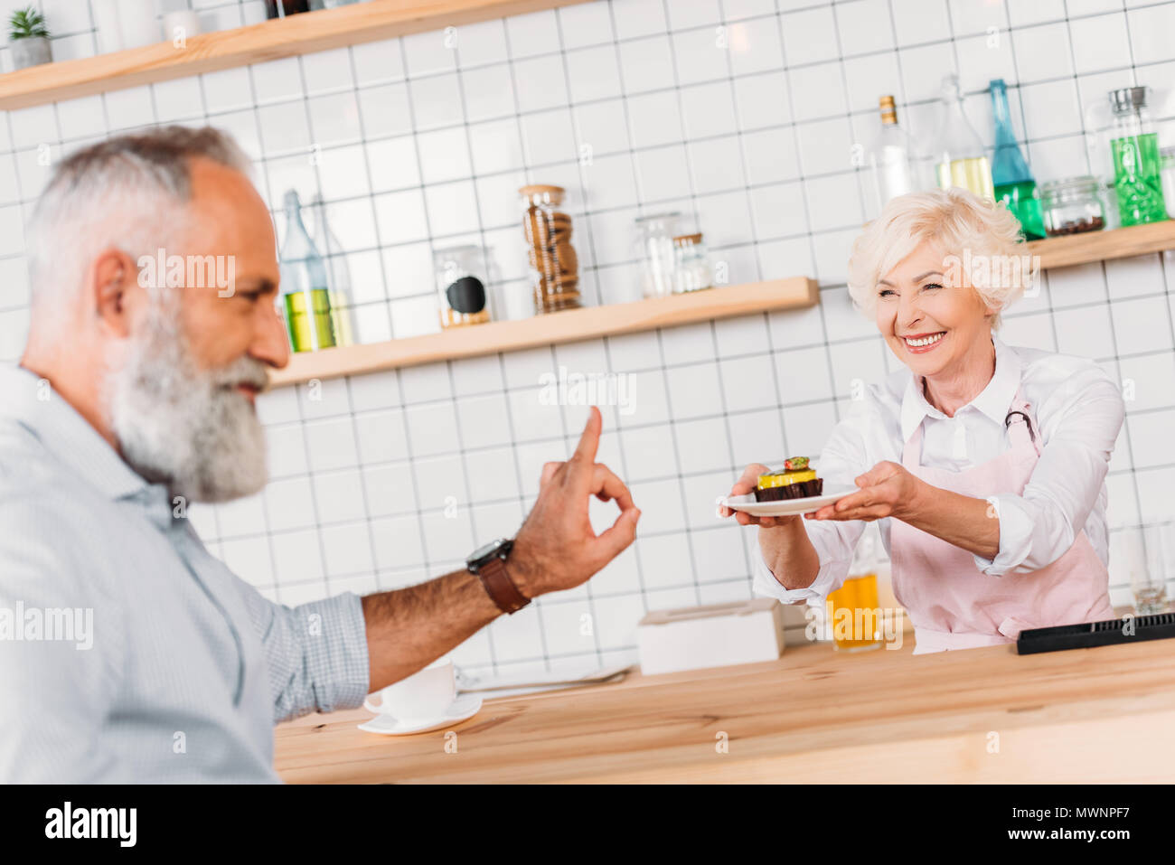 selective focus of smiling cafe worker offering pastry to senior man at ...