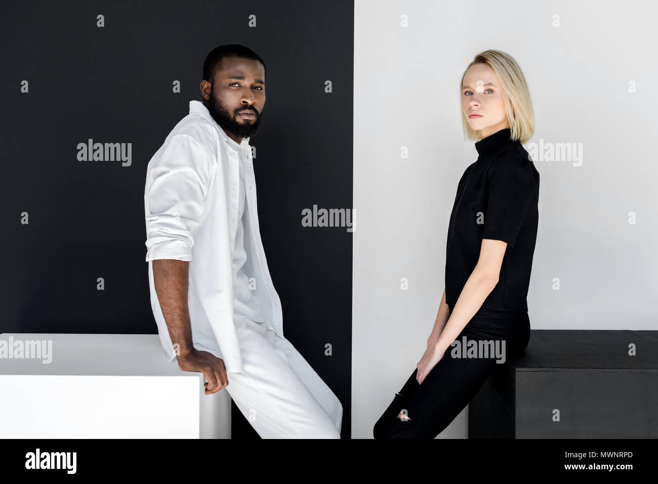 side view of multicultural couple sitting on black and white cubes ...