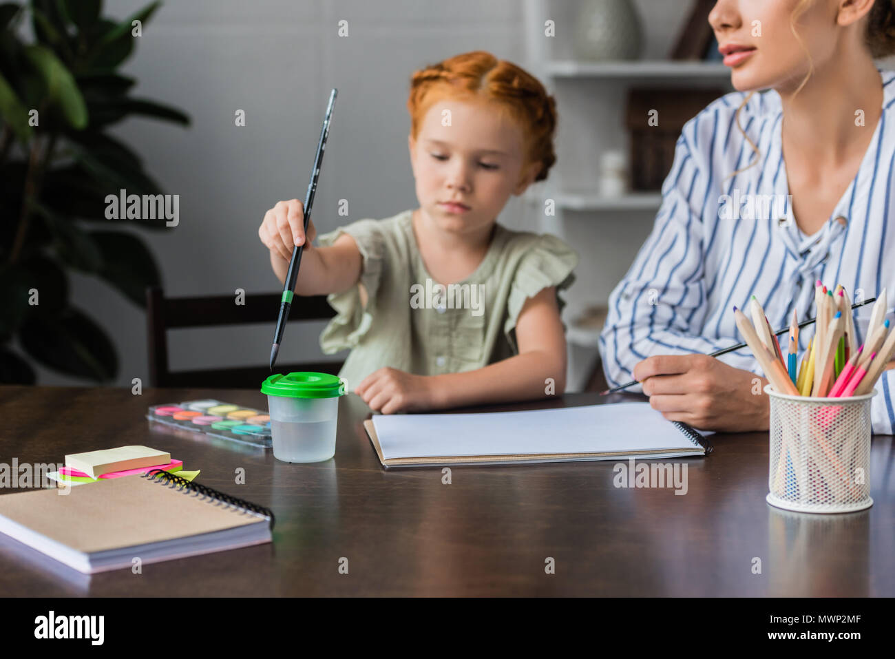thoughtful mother and cute little daughter drawing in album Stock Photo ...