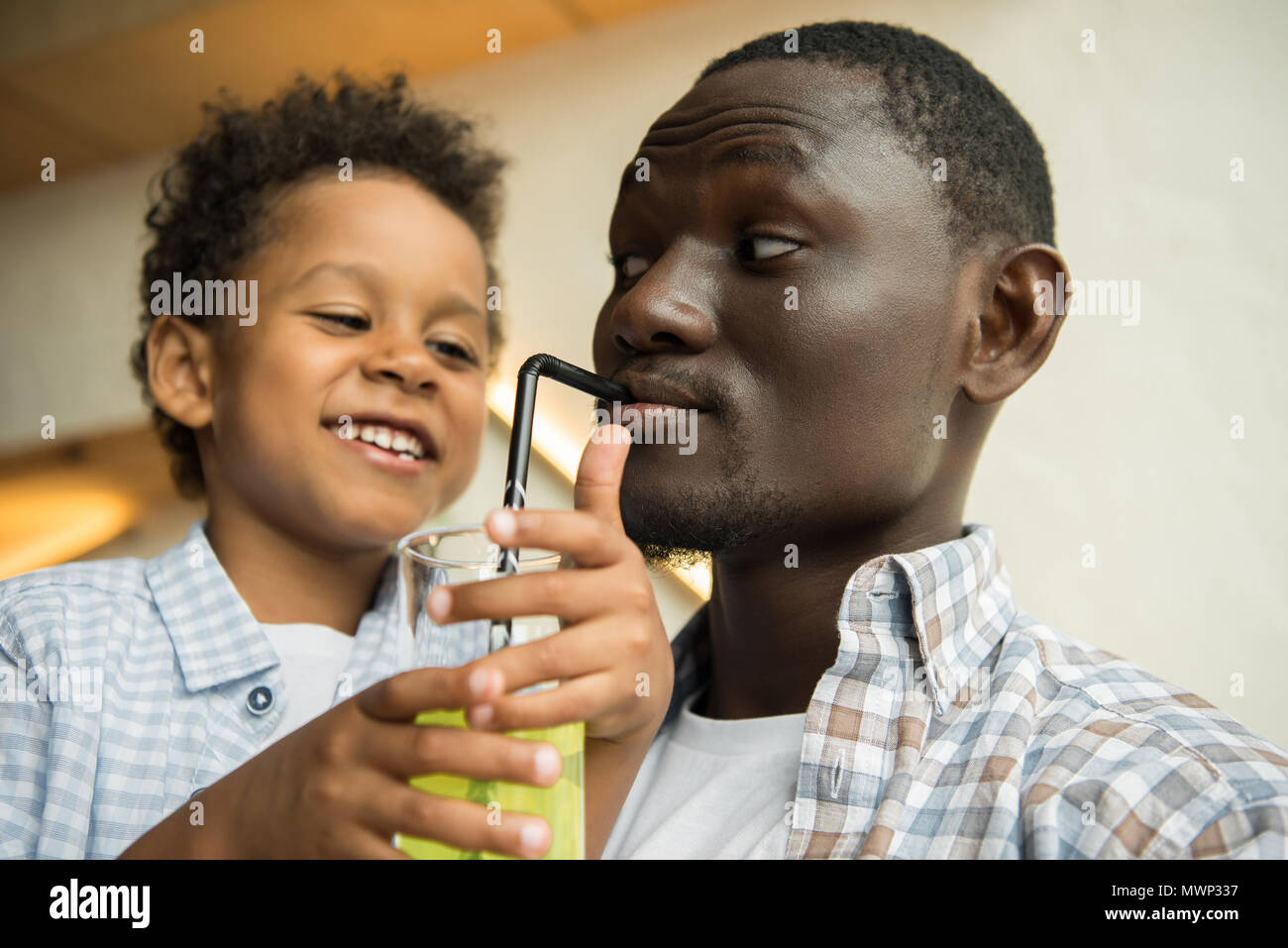 young african american man drinking lemonade while cute little son ...