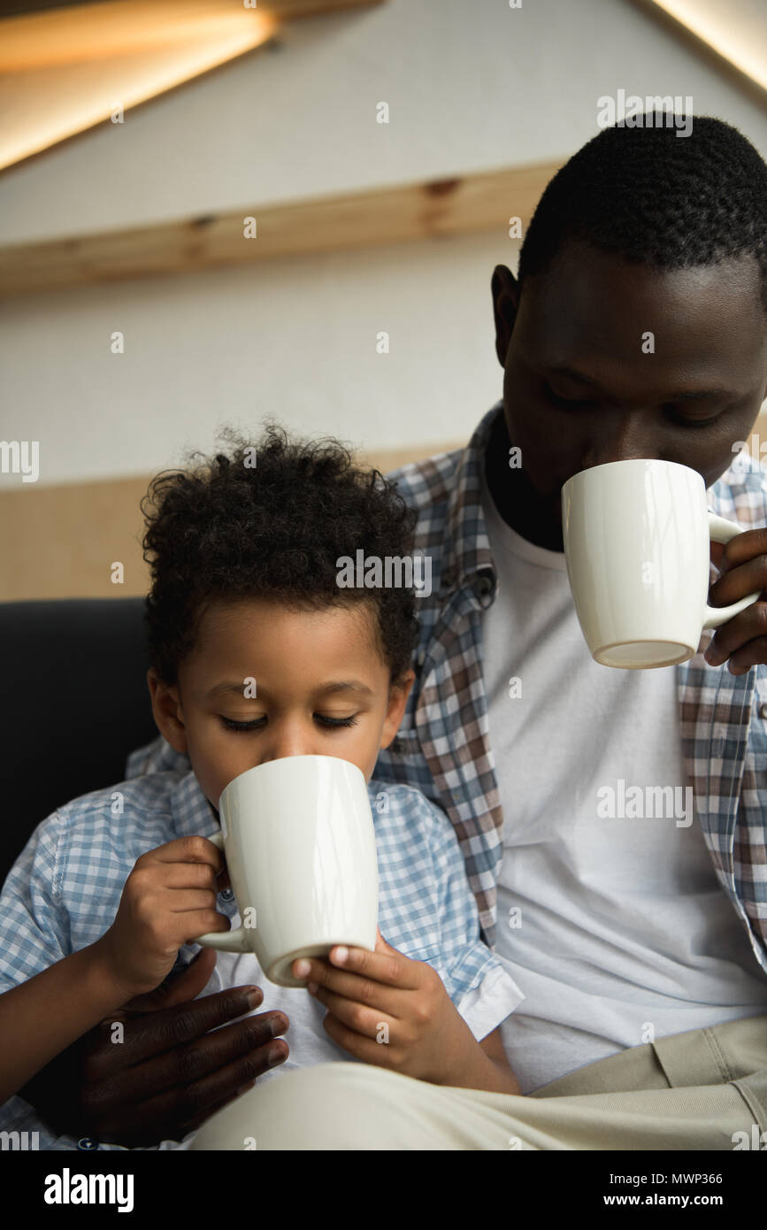 african american father and son drinking tea while sitting together in ...