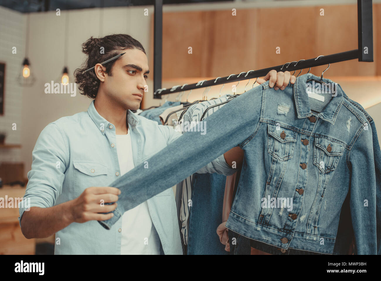 serious young shop owner holding denim jacket in boutique Stock Photo ...