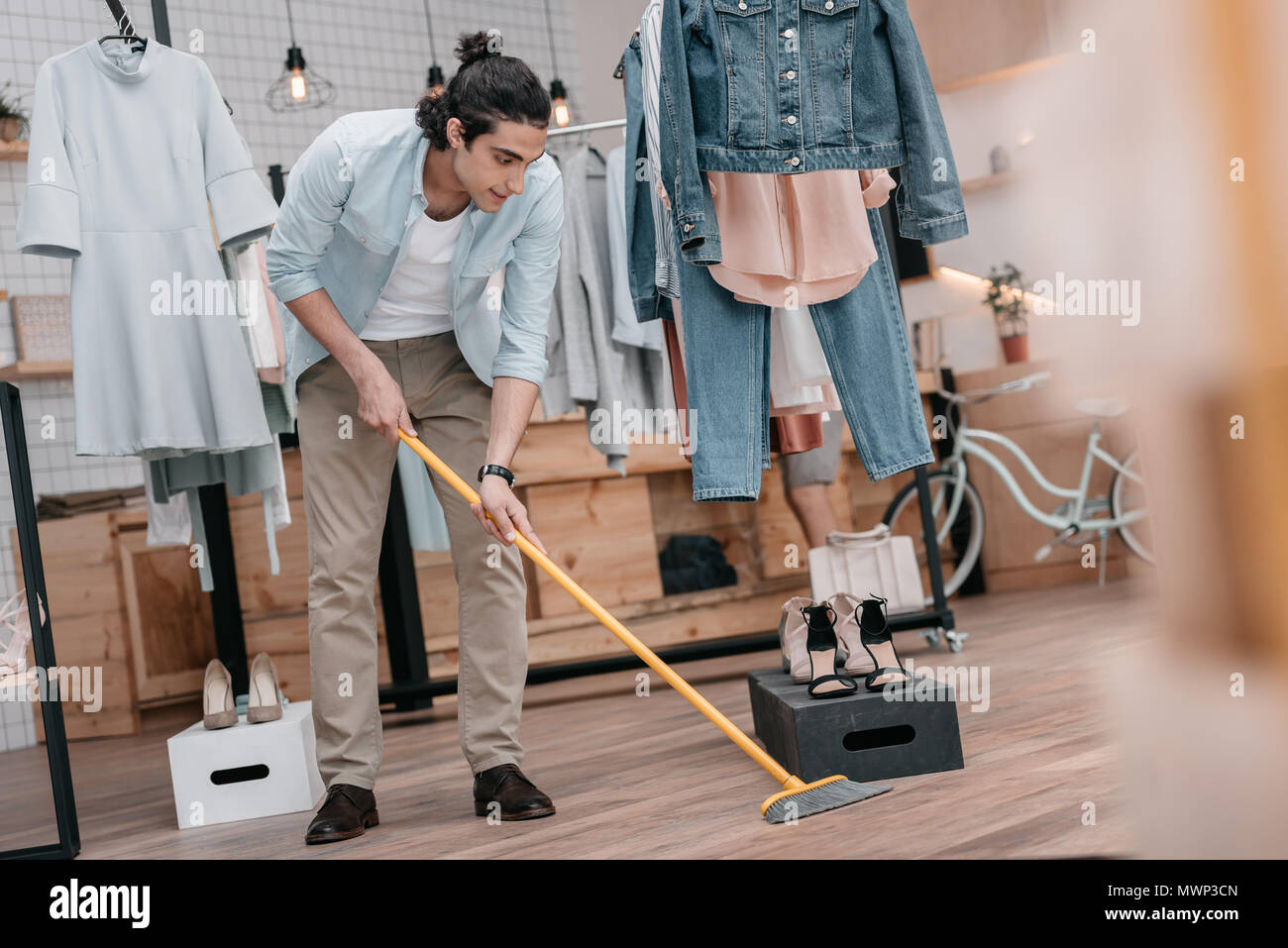 handsome young man with broom sweeping floor in shop before opening ...