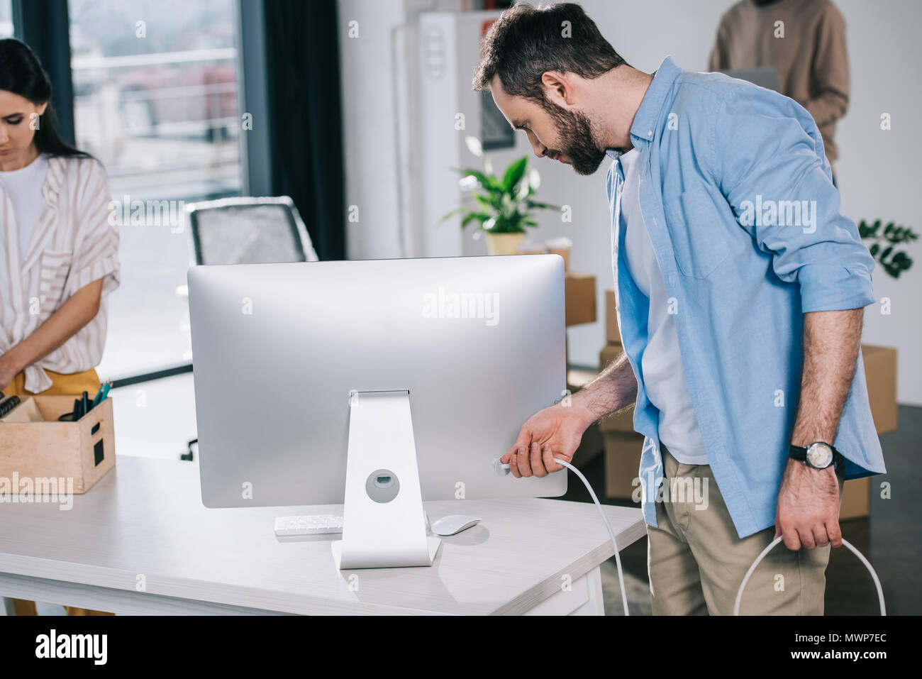 man holding plug from desktop computer while relocating with coworkers ...