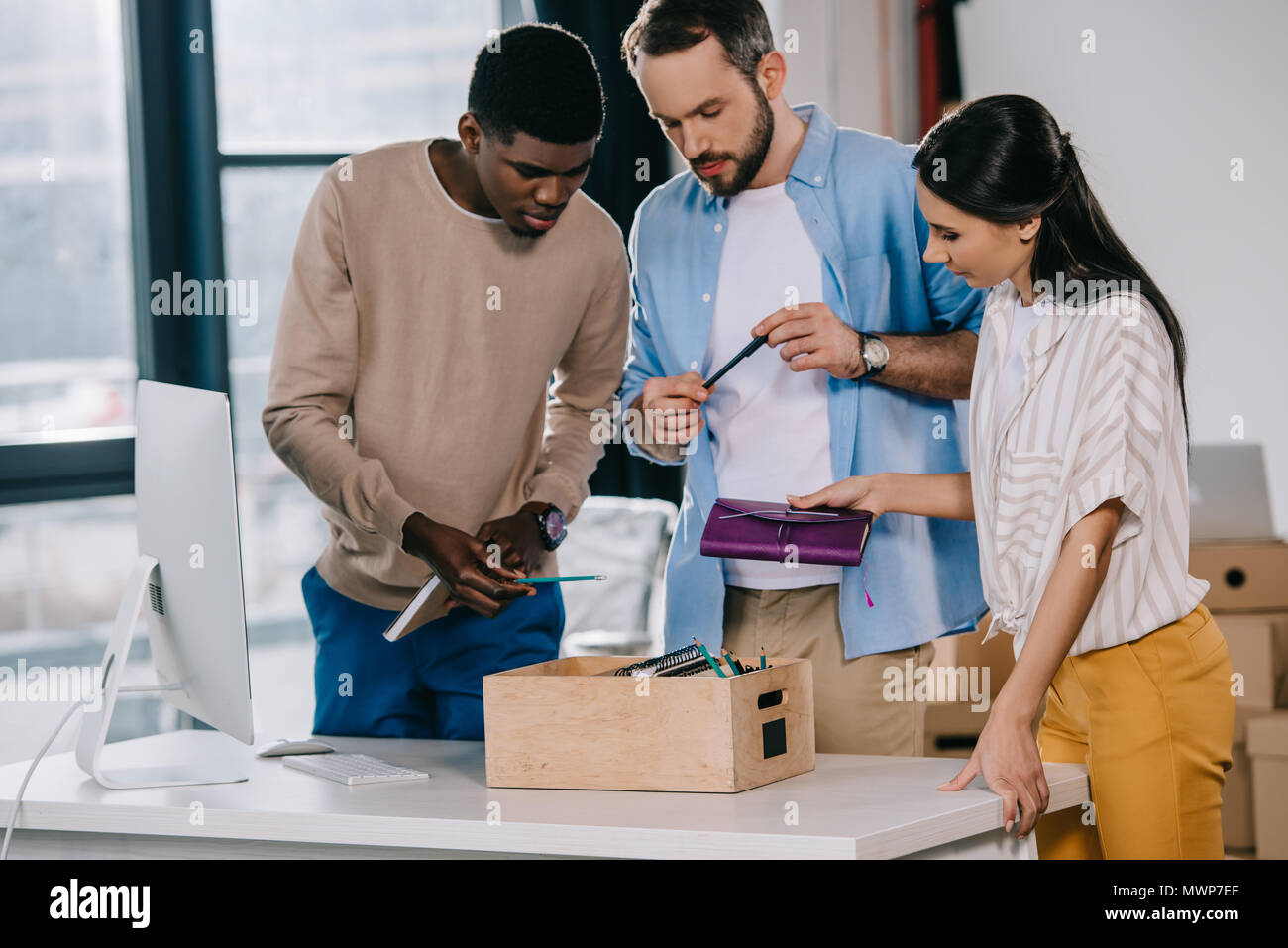 multiethnic coworkers unpacking box with office supplies at new ...