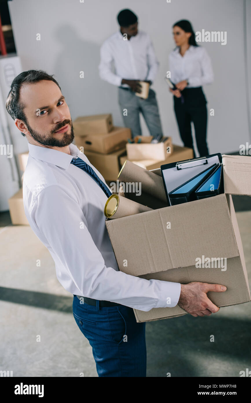 businessman holding cardboard box with office supplies and looking at ...