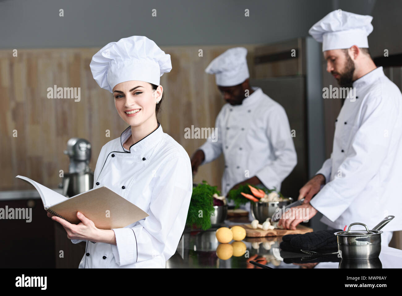Female chef checking recipe in book by her multiracial colleagues Stock ...