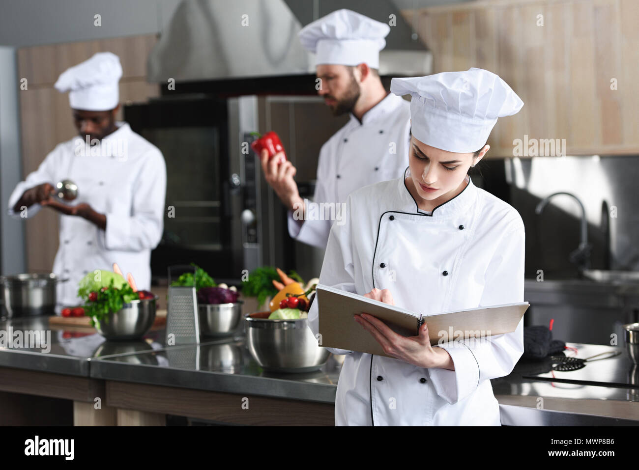 Female chef writing in recipe book by her multiracial colleagues Stock ...